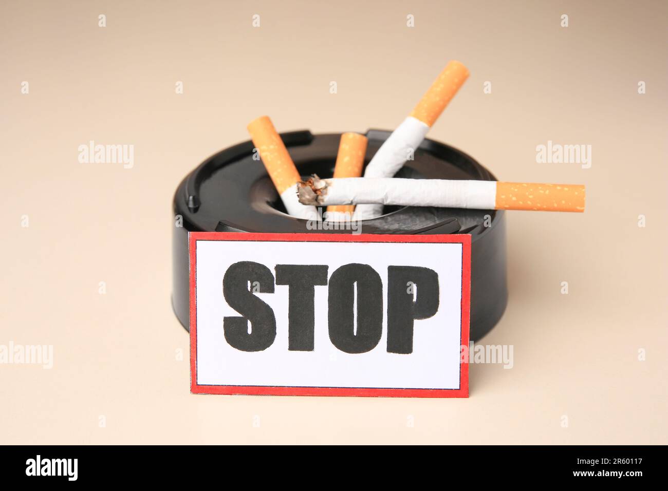 Card with word Stop, ashtray and cigarette stubs on beige background ...