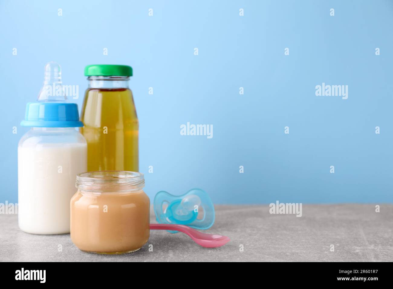 Jar with healthy baby food, milk, juice, pacifier and spoon on light ...