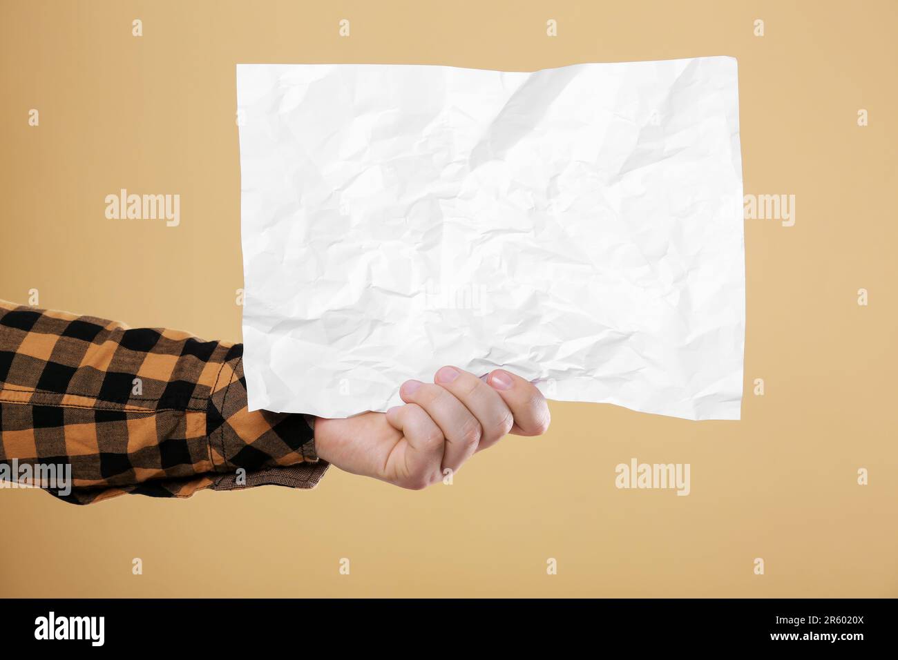Man holding sheet of crumpled paper on pale orange background, closeup ...