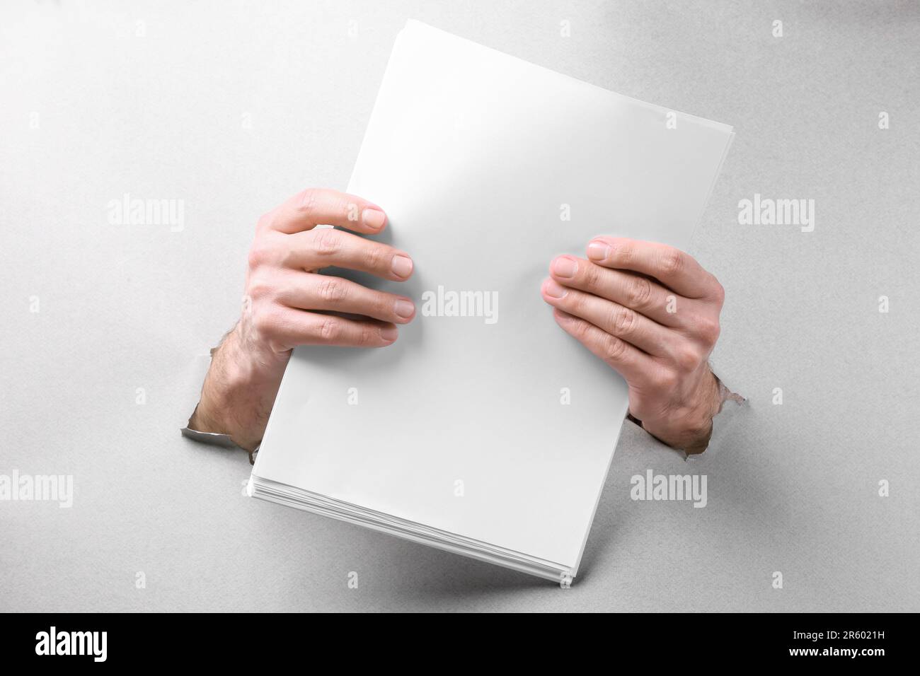 Man holding sheets of paper through holes in white paper, closeup ...