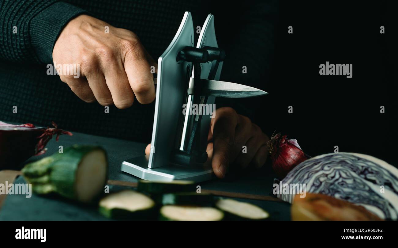 man sharpening a kitchen knife with a desktop sharpener on a table, in ...