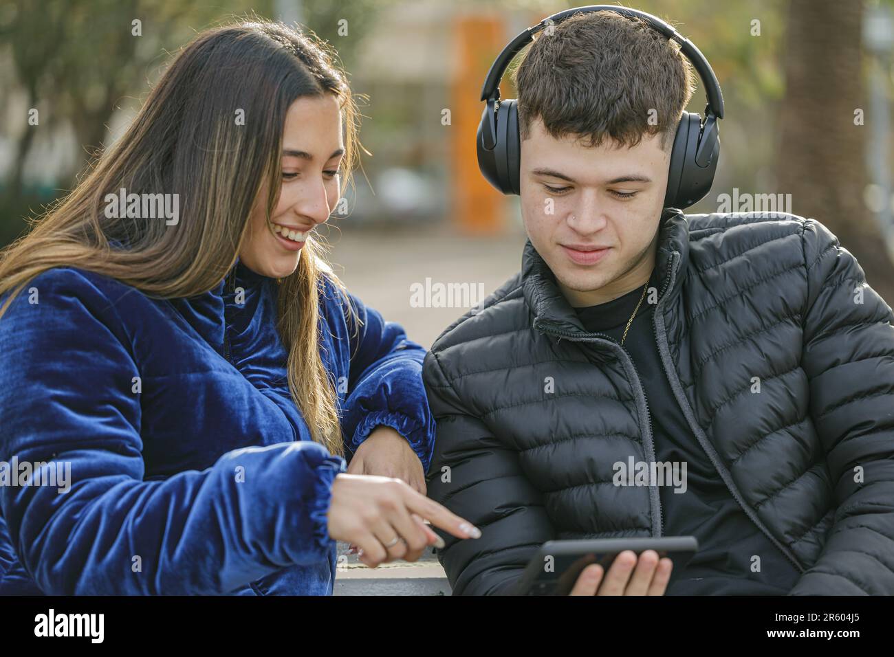 Young couple sitting on the bench in a square with mobile phone and ...