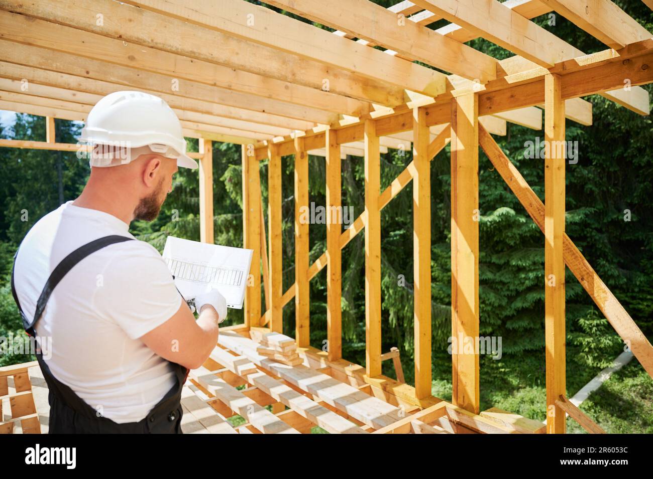 Builder constructing wooden two-story structure near forest. Back view ...