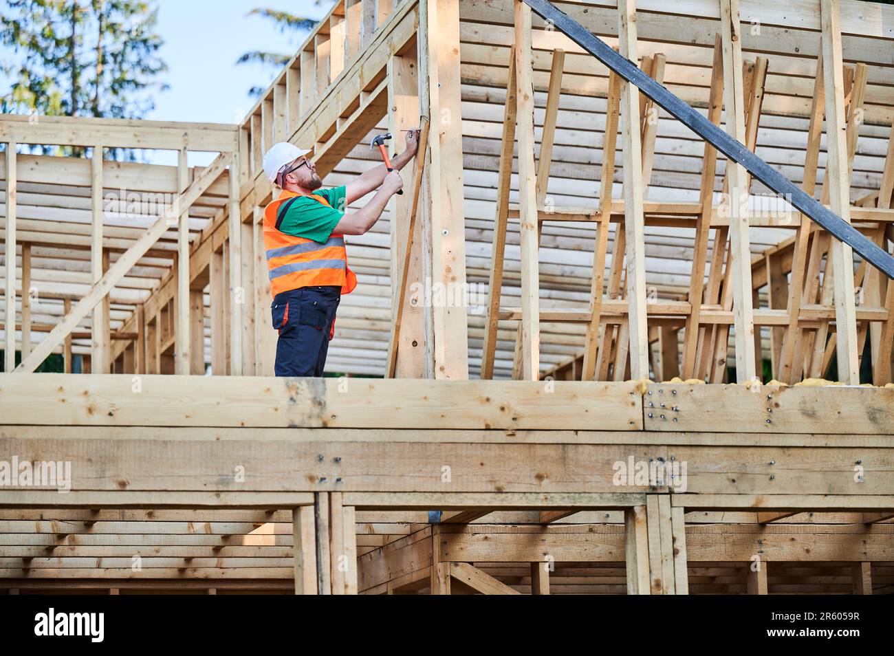 Carpenter constructing two-story wooden frame house near the forest ...