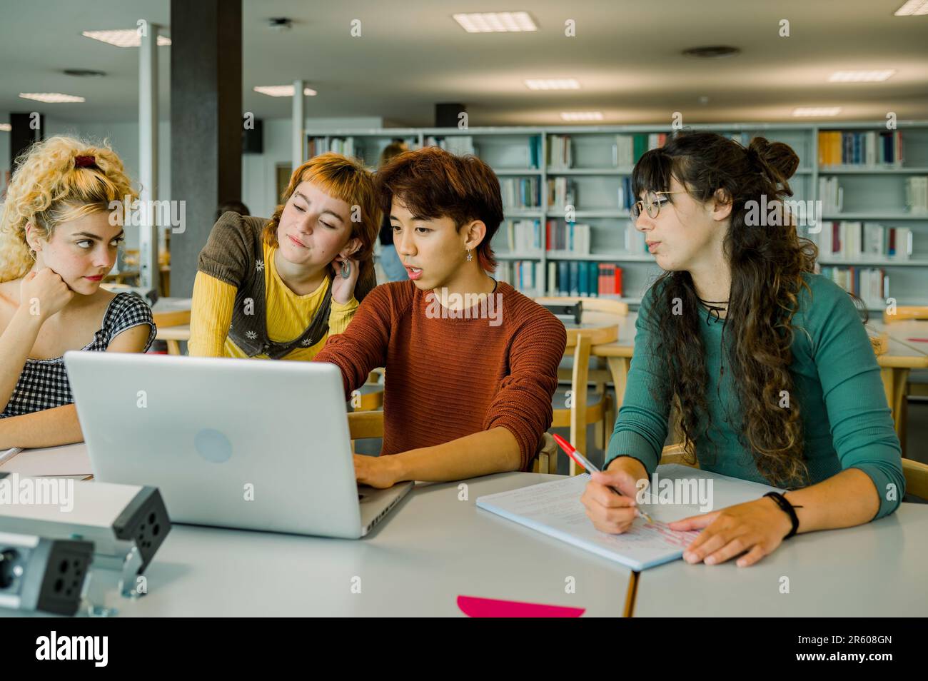 Diverse students working on laptop for project in library Stock Photo ...