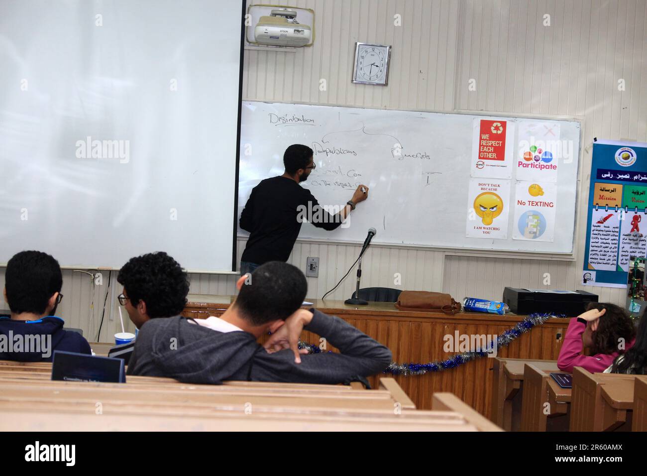 Classroom scene with a teacher writing on a whiteboard and students ...