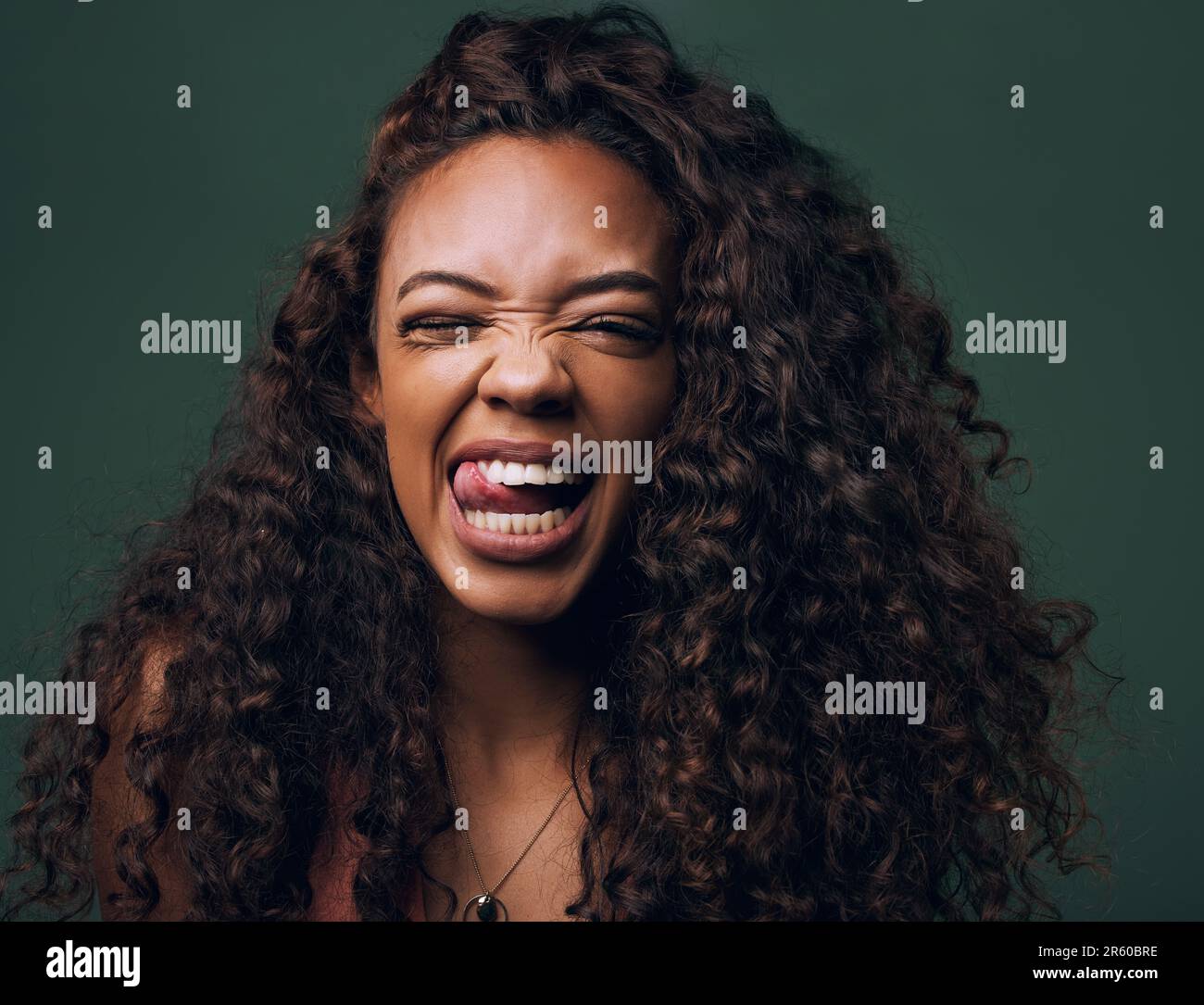 Tongue out, portrait and young woman in studio with natural curly hair ...