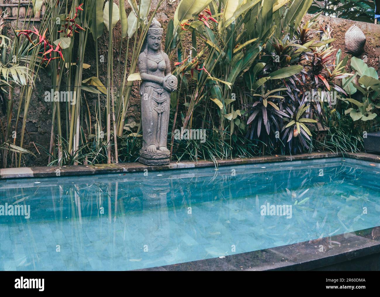 A bronze statue of a figure situated beside a pool of water, with lush ...