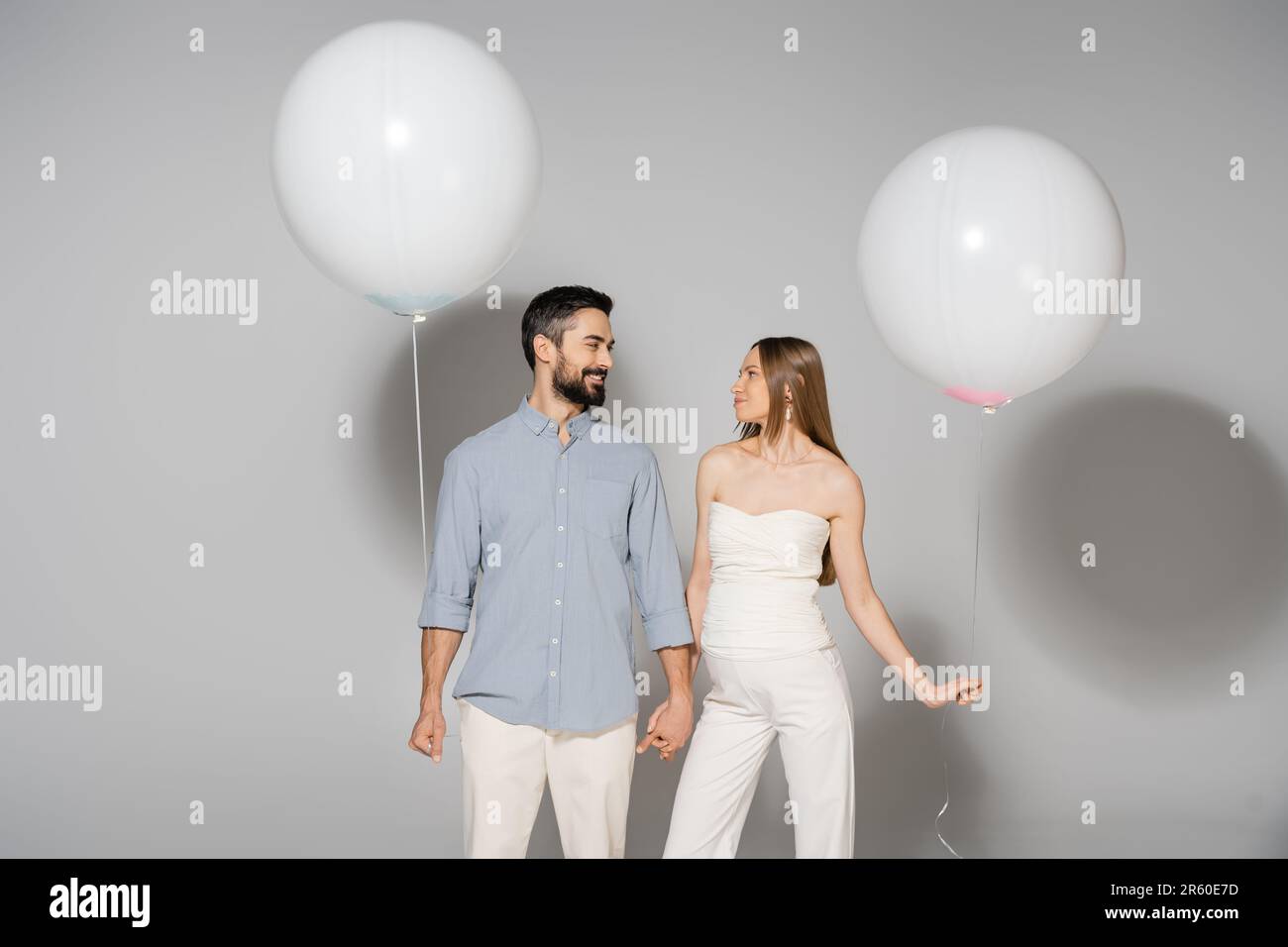 Positive and trendy expecting parents holding hands and festive ...