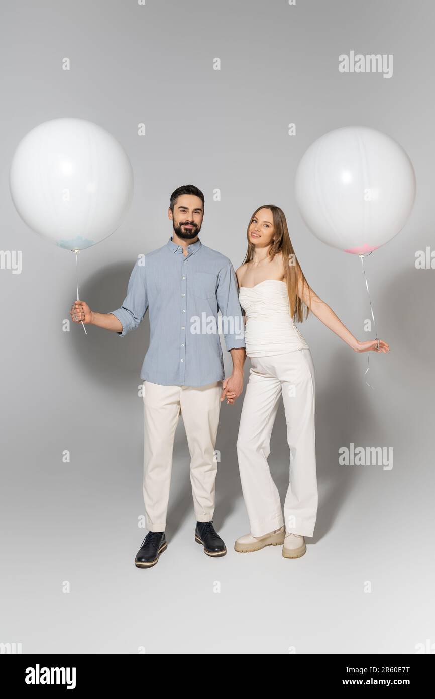 Full length of fashionable and happy expecting parents holding white ...