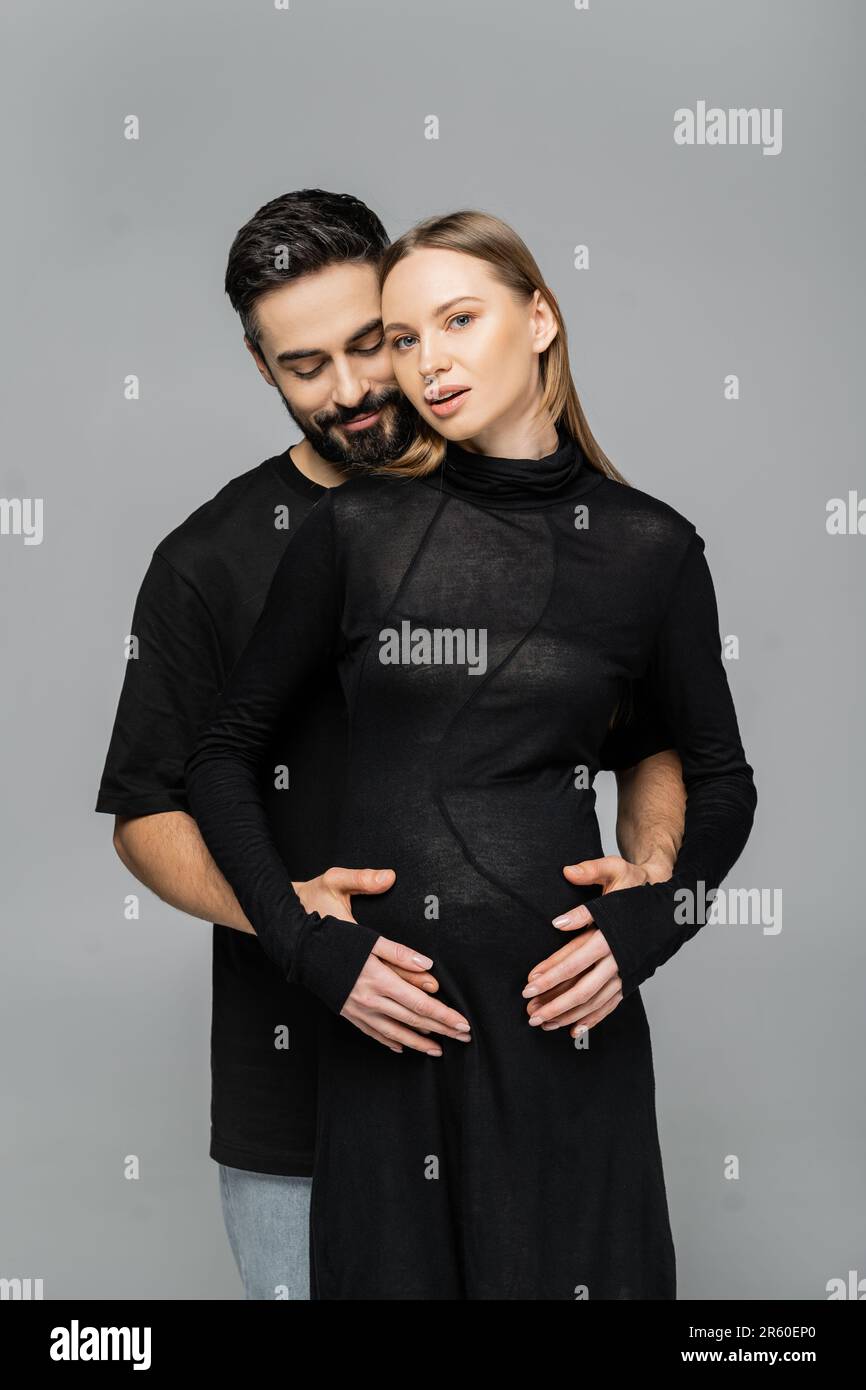 Bearded man in black t-shirt touching belly of stylish and pregnant ...