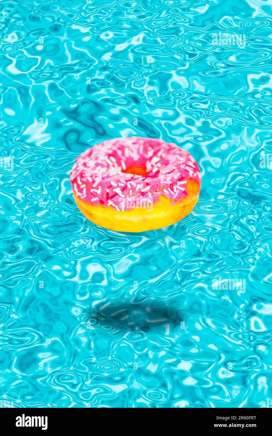 Donut with pink icing flies over the surface of the water in the pool ...