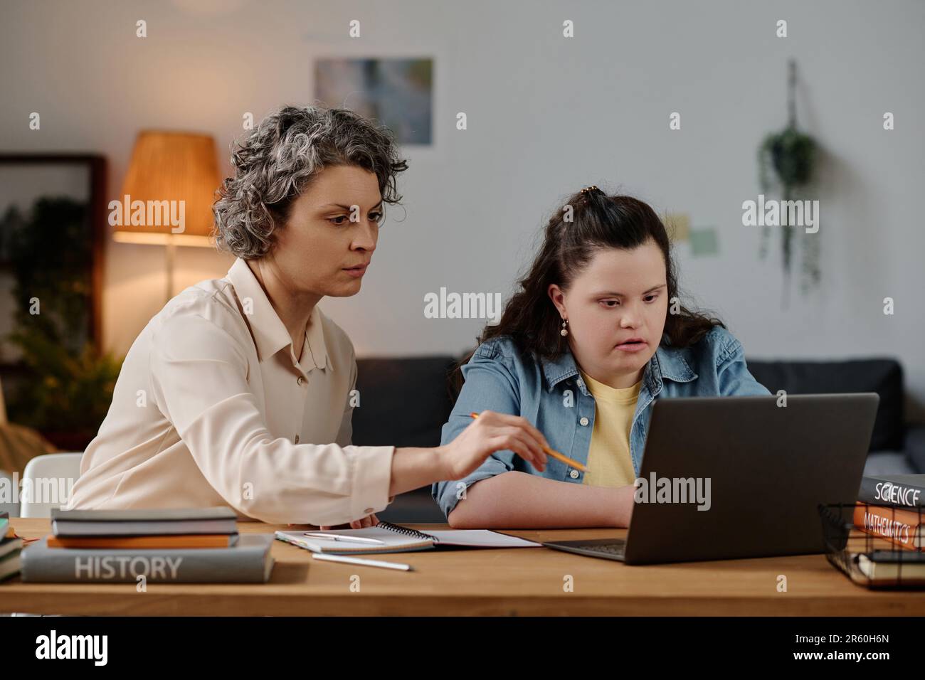 Tutor pointing at monitor of laptop and teaching girl with down ...