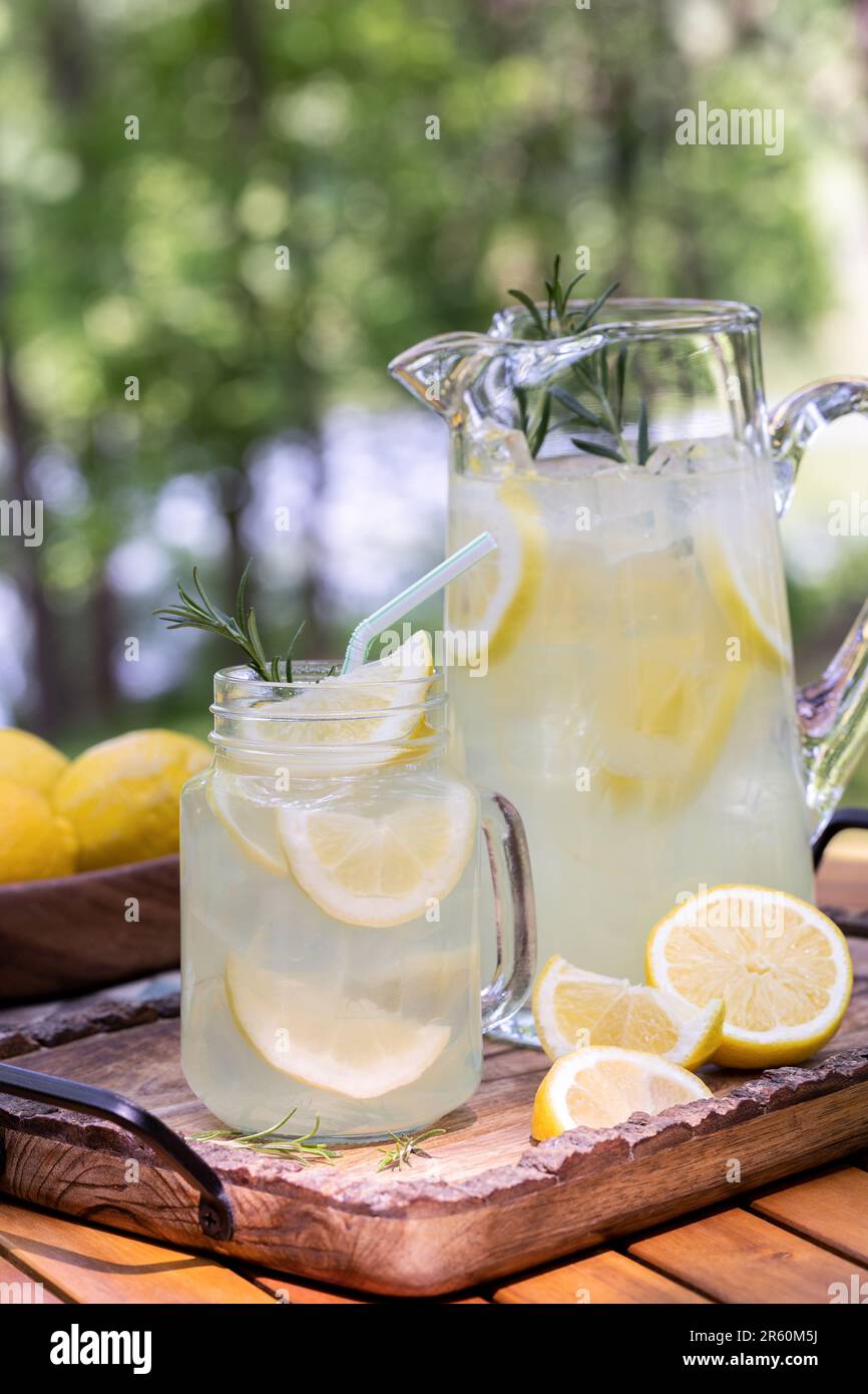 Glass and pitcher of lemonade with lemon slices and rosemary on wooden ...