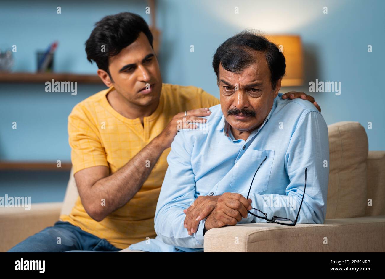 Adult son consoling senior or elderly father at home while sitting on ...