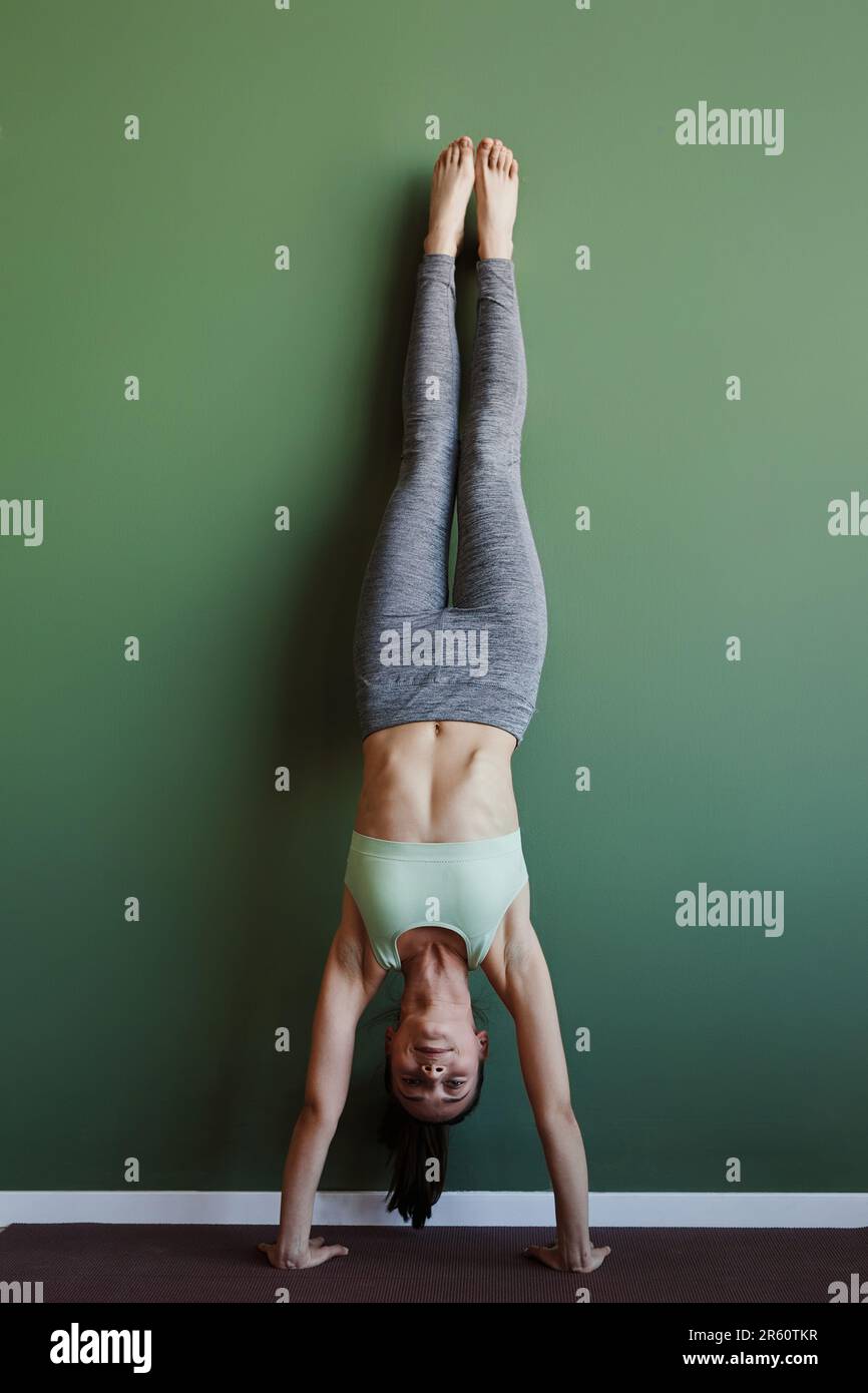 Vertical full length portrait of fit young woman doing handstand ...