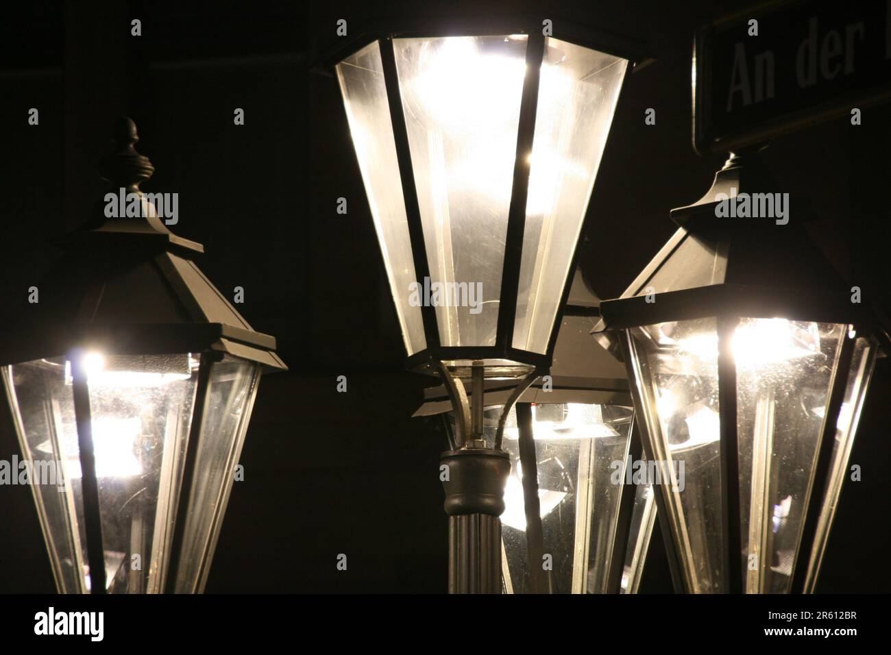 Three traditional style street lights illuminating a street sign at ...