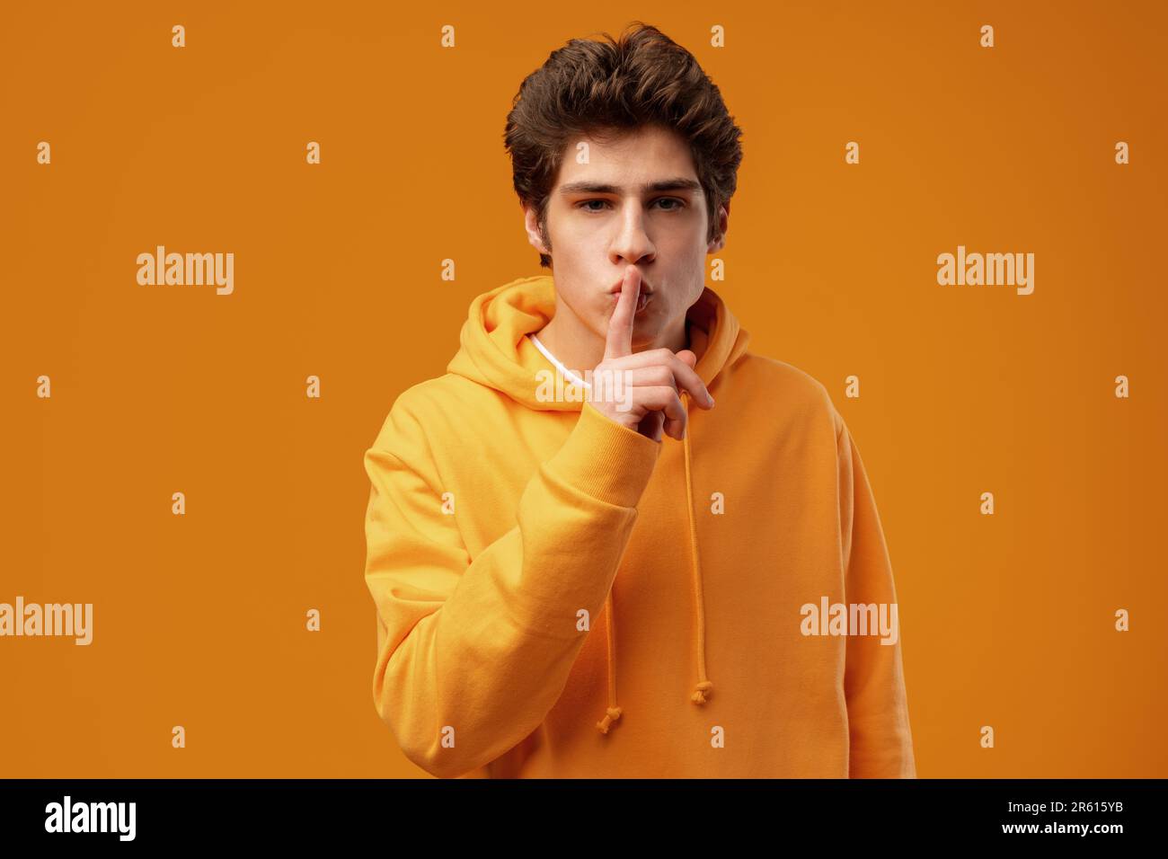 Young man hushing at camera and telling to be quiet on yellow ...