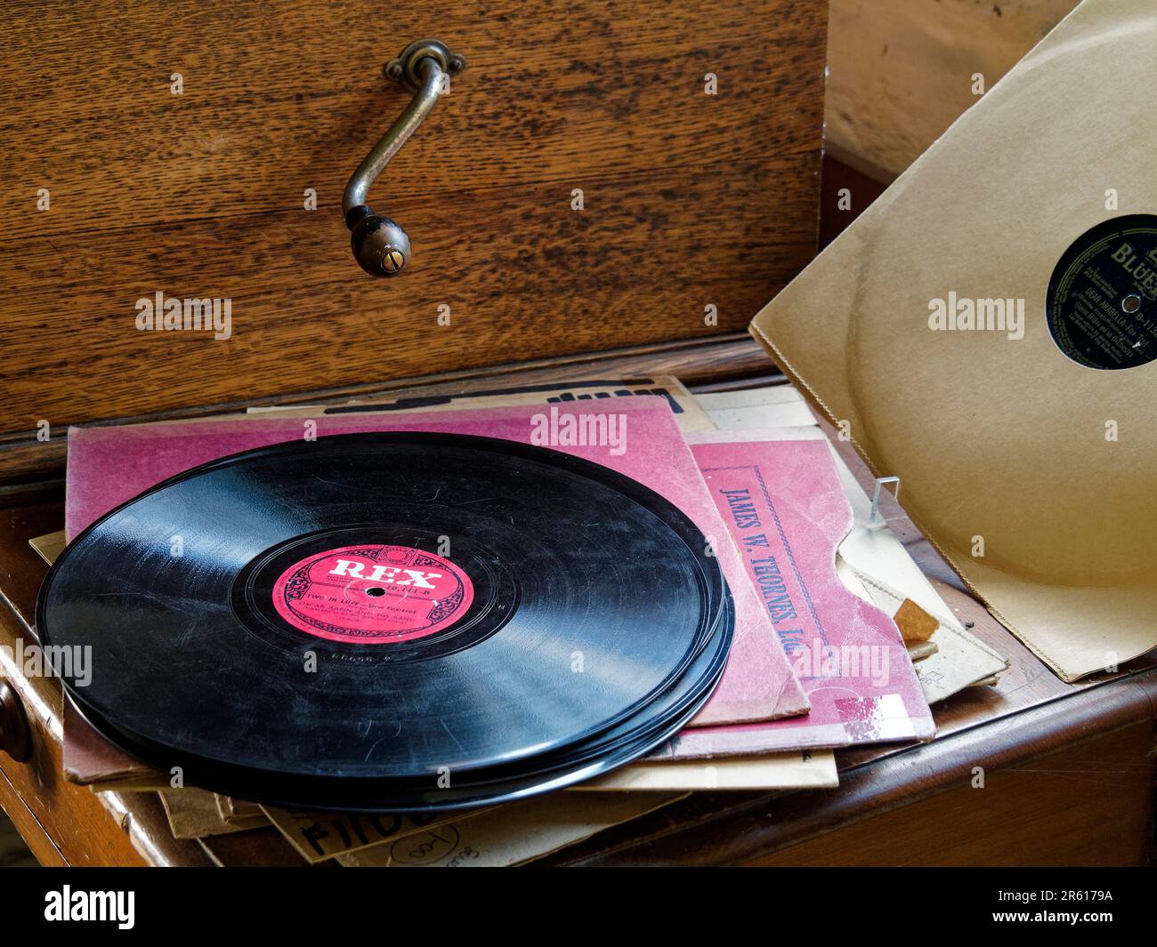 Old style 78 rpm records (78s), some in their sleeves, alongside a wooden wind-up gramophone as ...