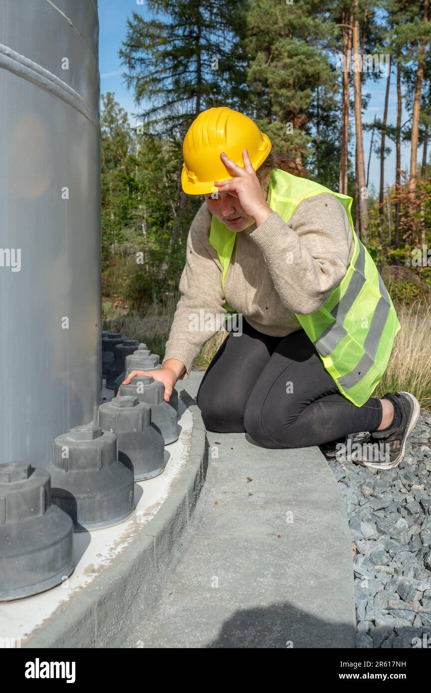 An engineer woman wearing a hard hat inspecting a series of gray pipes ...