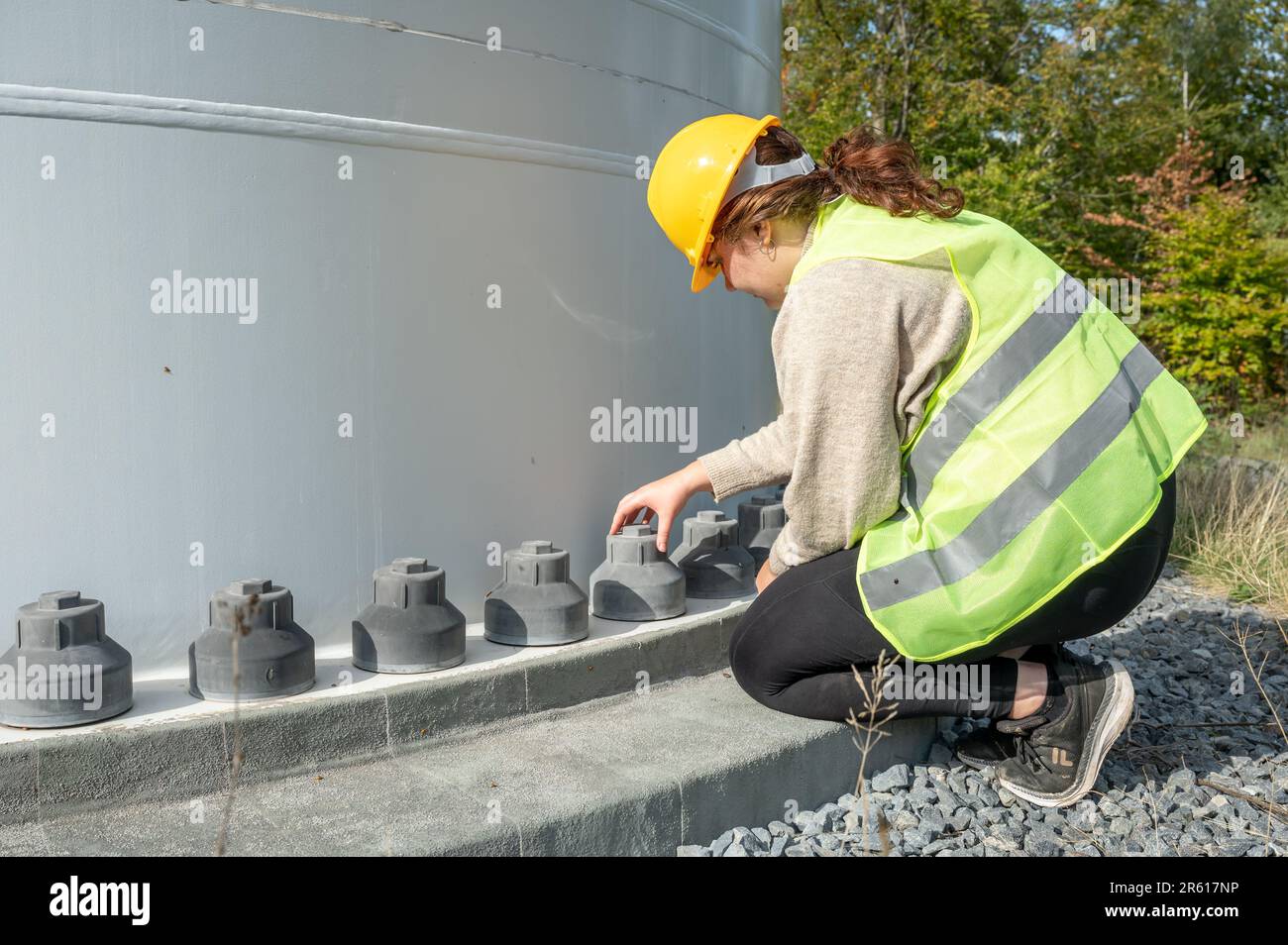 An engineer woman wearing a safety vest inspecting a series of pipes ...