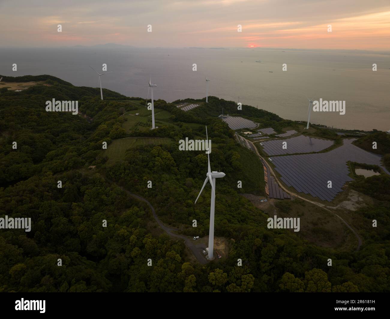 Wind turbines and solar panels on coast as sun sets over ocean Stock ...