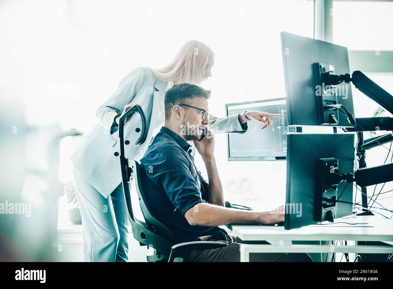 Two thoughtful business colleagues looking at data on multiple computer ...