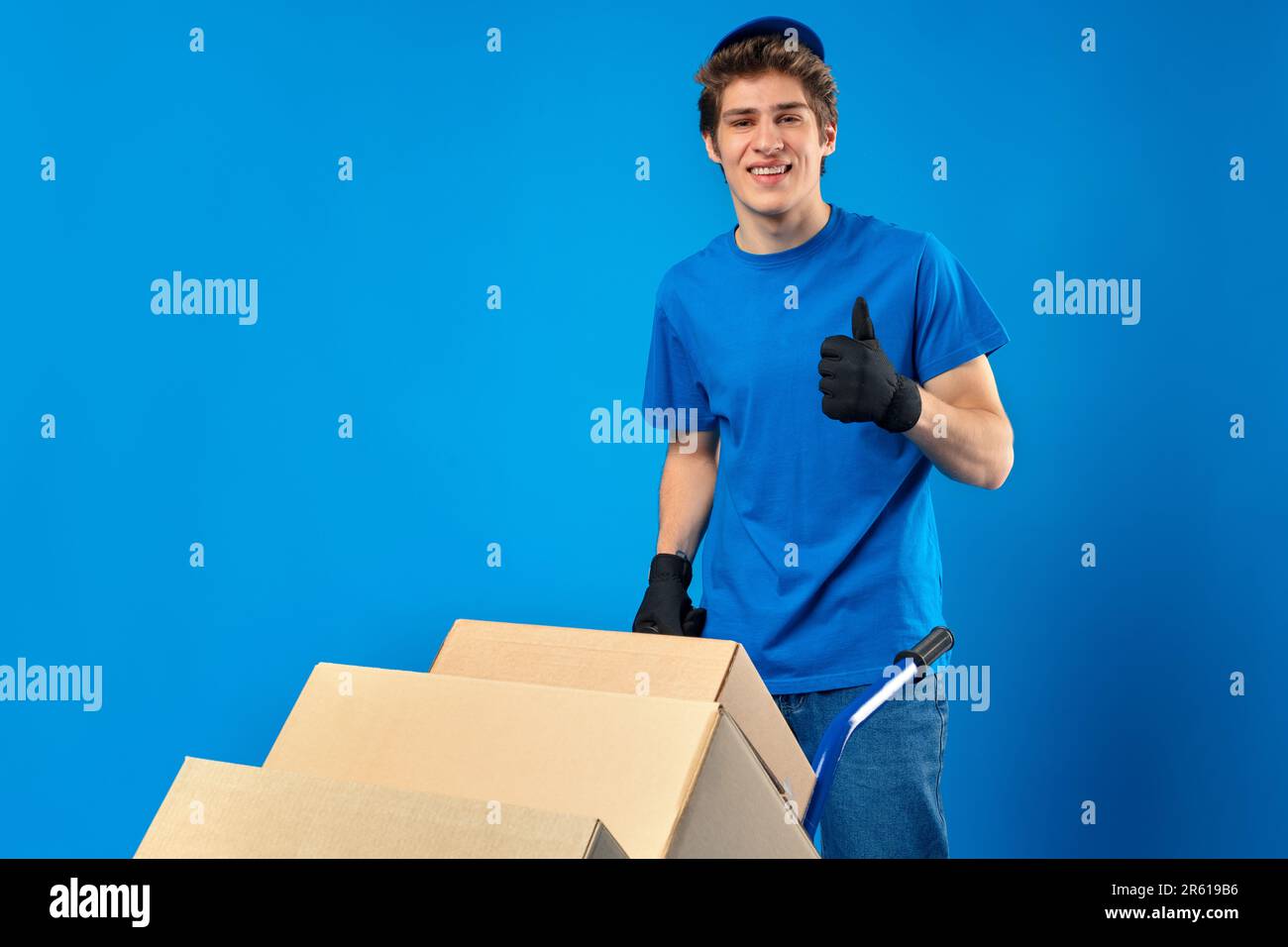 Young happy delivery man carrying boxes on truck against blue ...