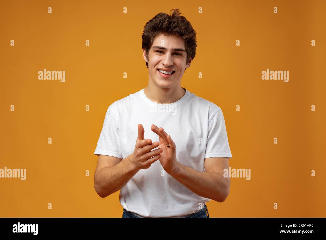 Portrait of cheerful young man clapping hands on yellow background ...