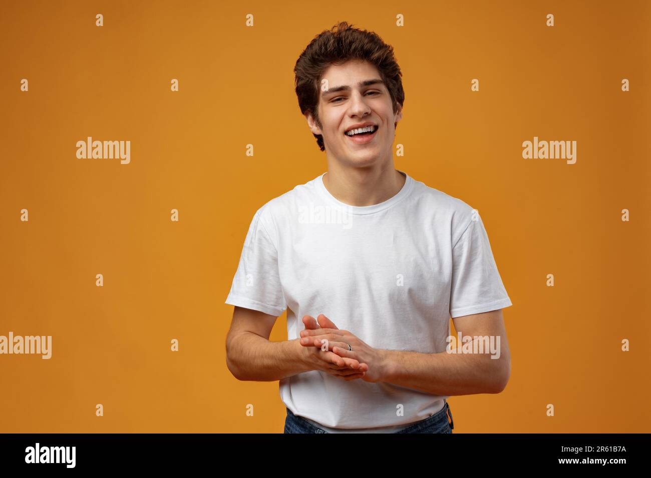 Portrait of cheerful young man clapping hands on yellow background ...