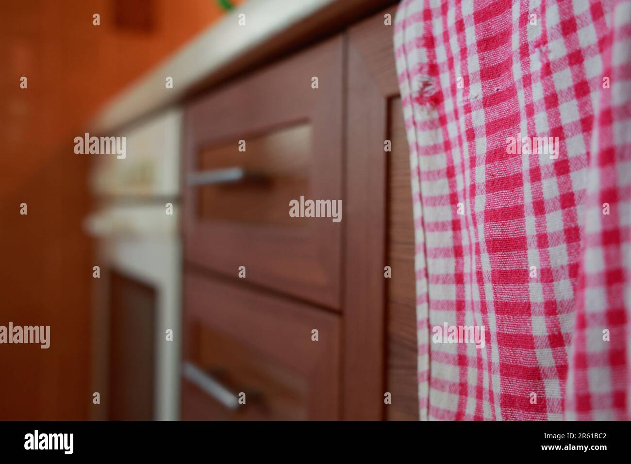 A pink and white checkered cloth draped over a wooden kitchen cabinet ...