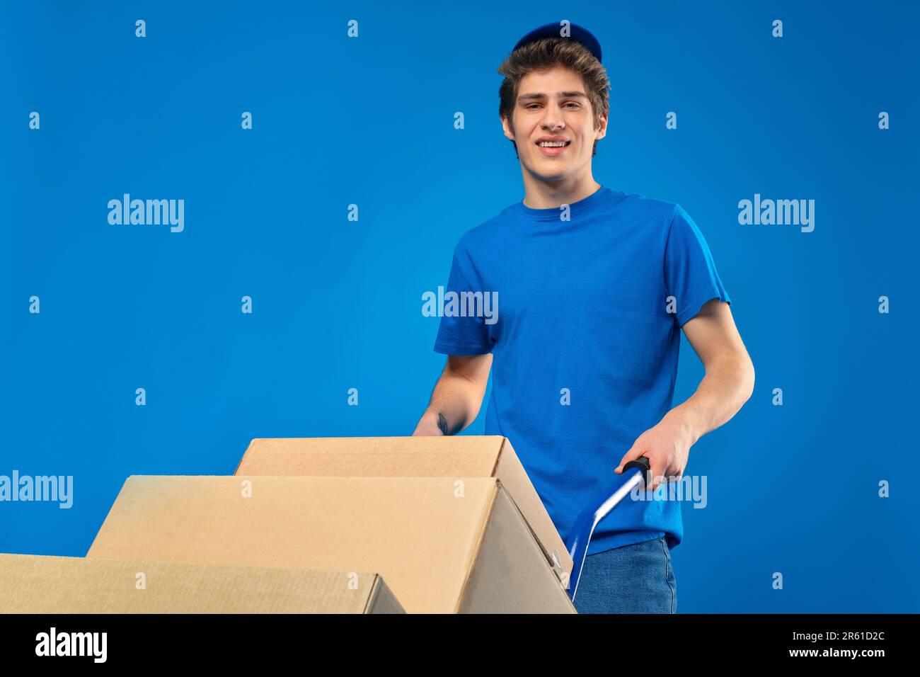 Young happy delivery man carrying boxes on truck against blue ...