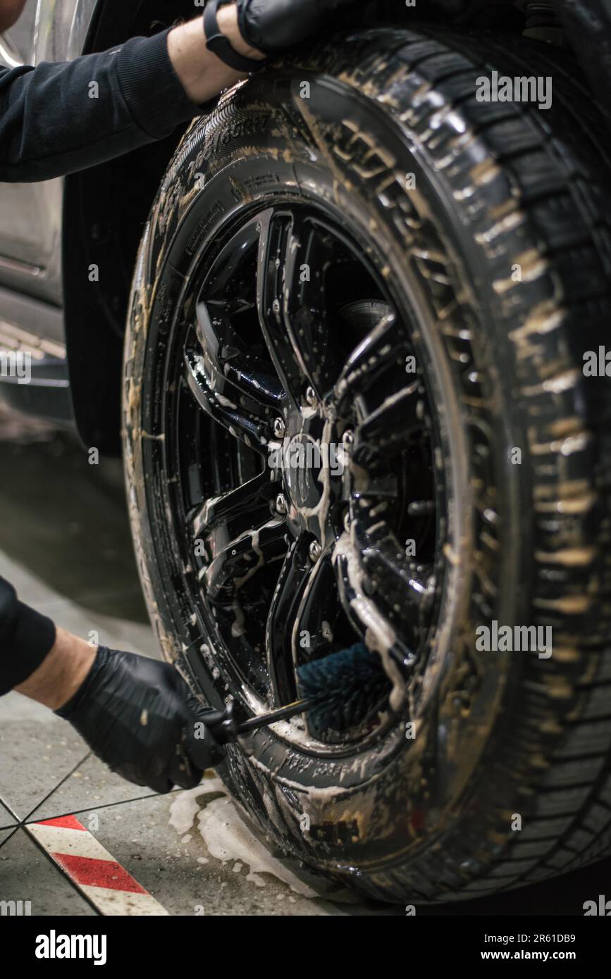 A closeup of a mechanic performing a detailed tire cleaning on a car's ...