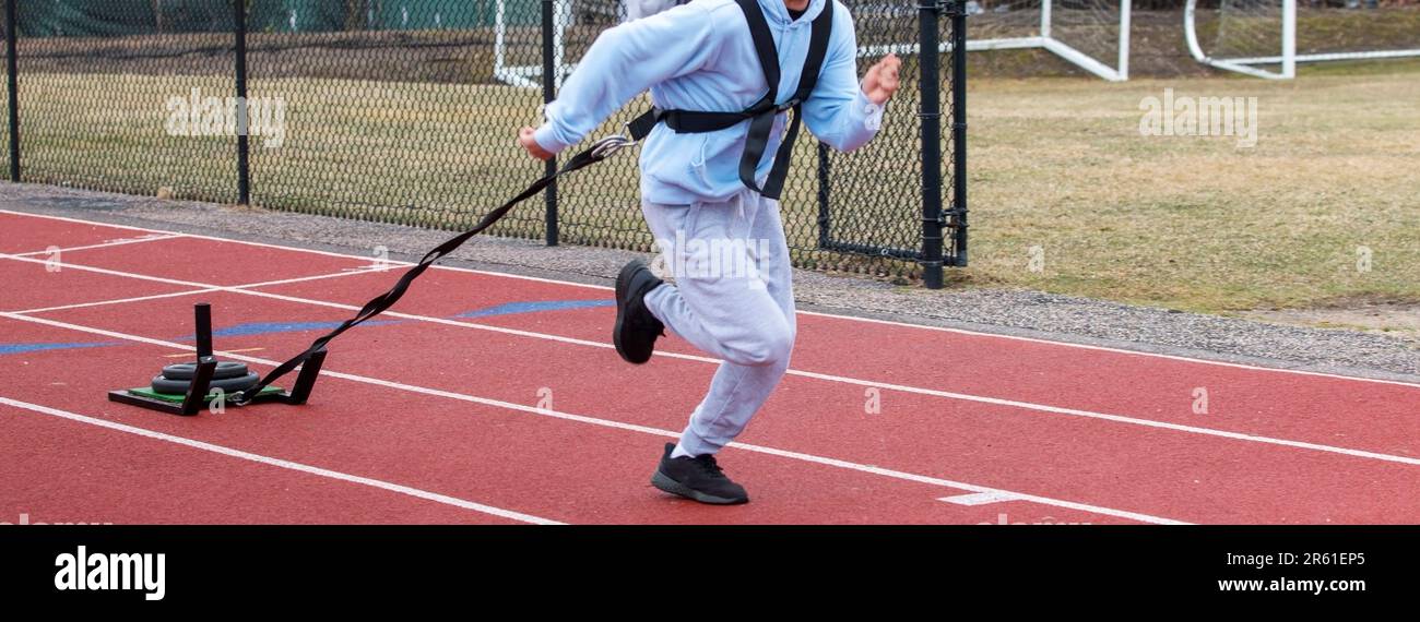 Athlete wearing sweats pulling a sled with weights on top while ...