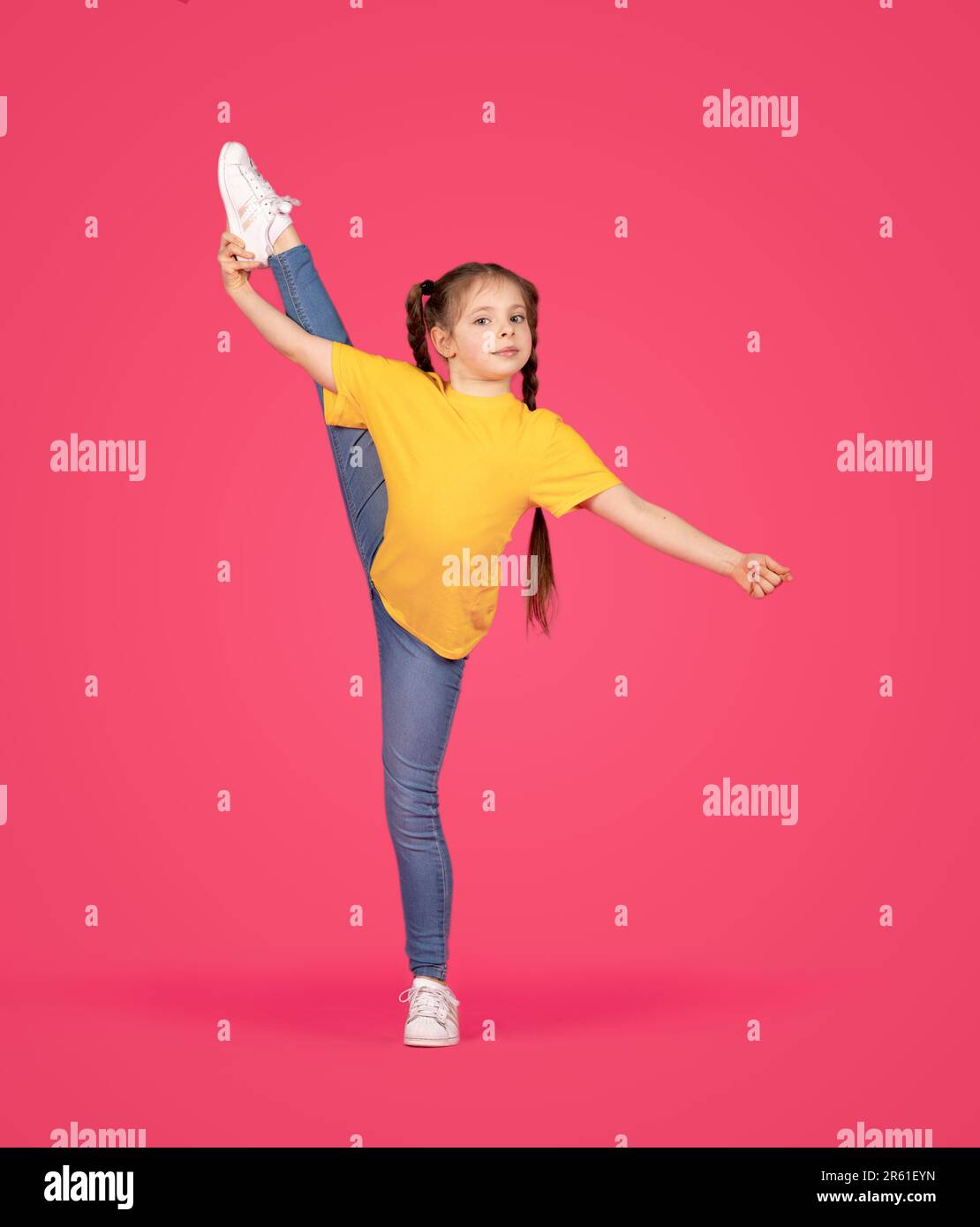 Sporty little girl making gymnastic exercises, raising her leg in twine ...