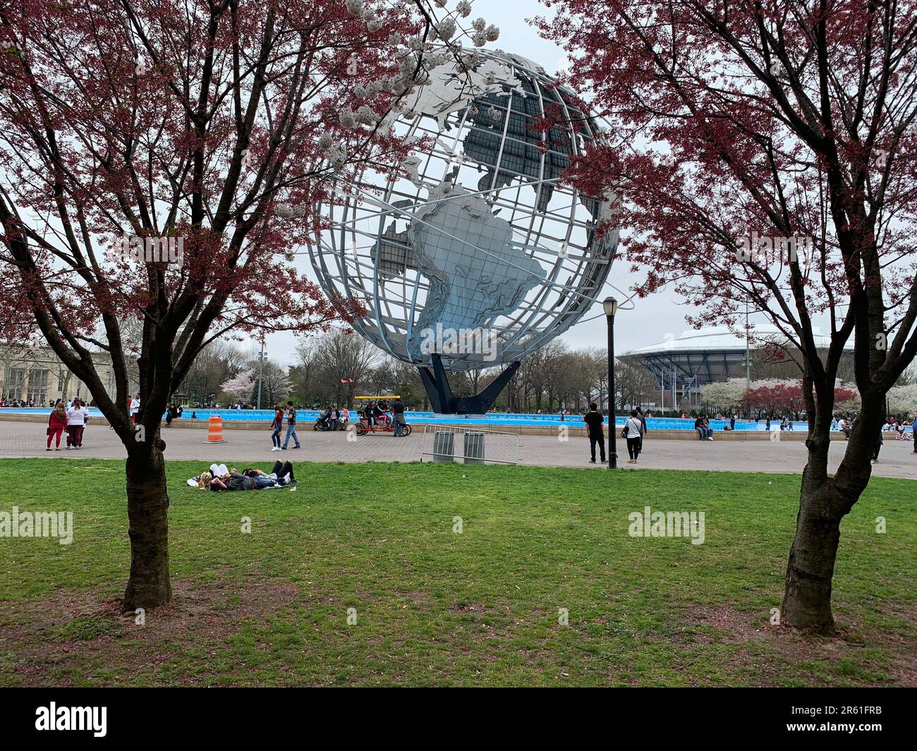 People lie on the lawn in front of the Unisphere and surrounded by ...