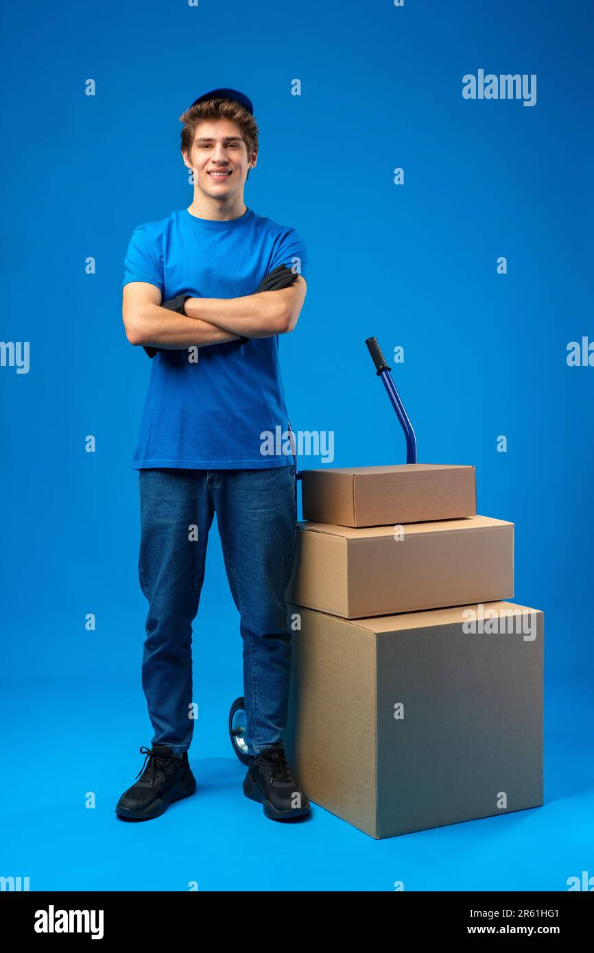 Young happy delivery man carrying boxes on truck against blue ...