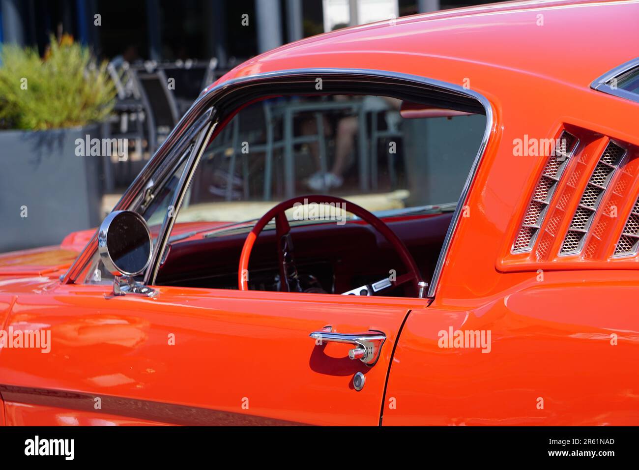 A vibrant orange classic car parked in the parking lot, with its sleek ...