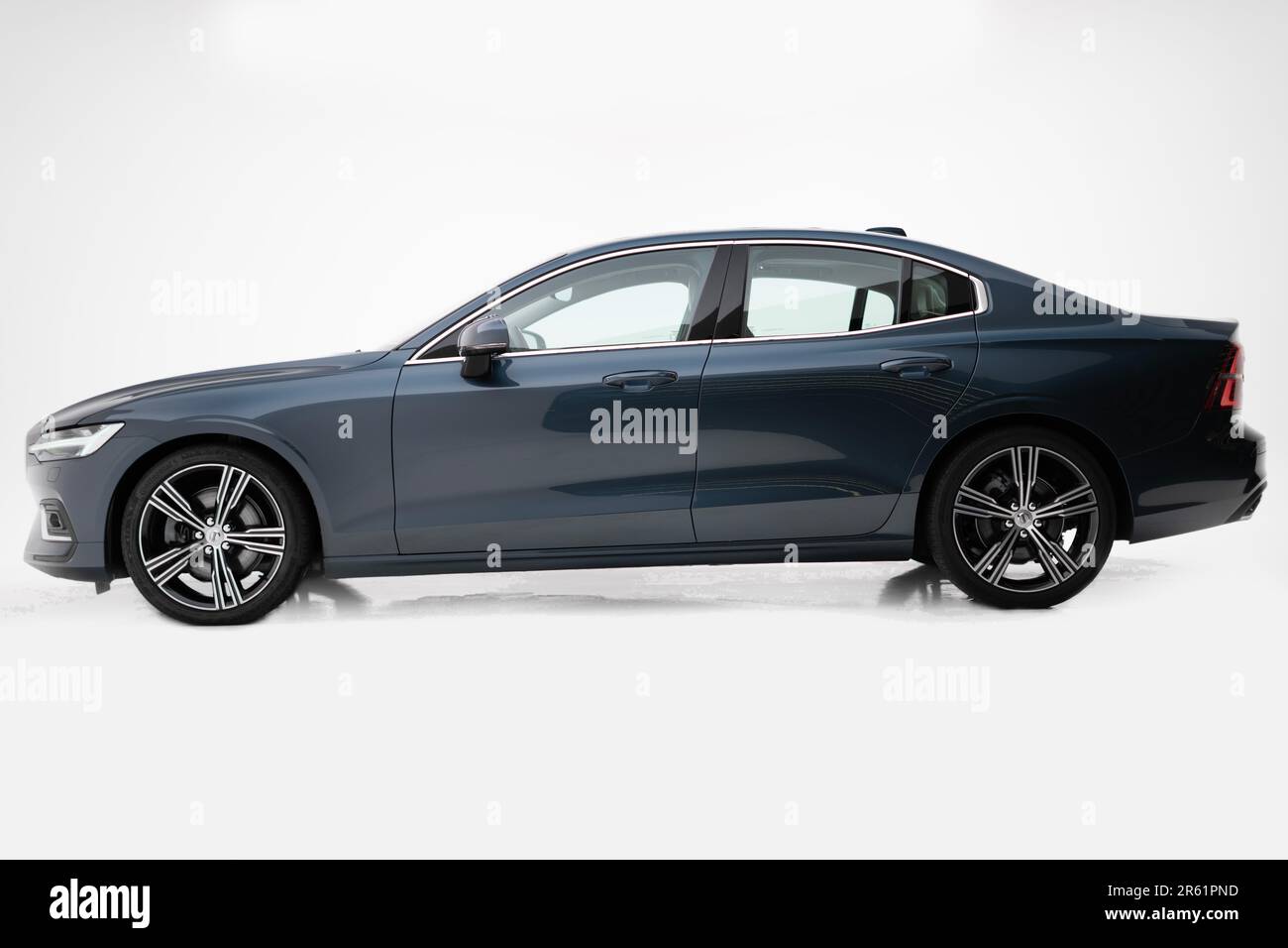 A modern, metallic blue Volvo sedan car parked against a plain white ...