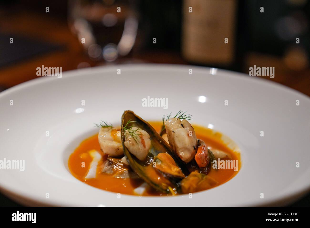 A bowl of steaming hot tomato-based seafood soup, garnished with herbs ...