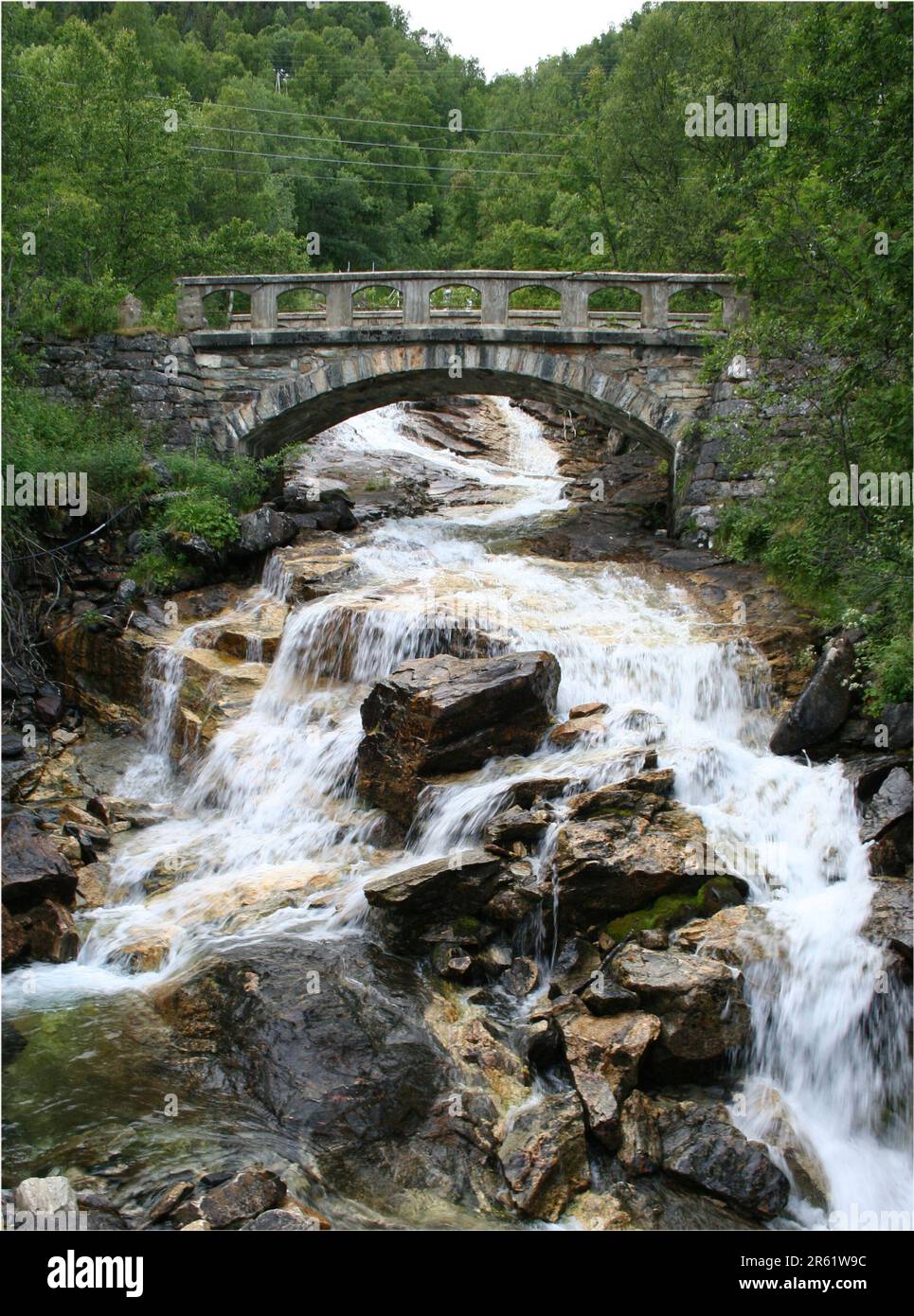 A stunning old stone bridge stands over a cascading waterfall ...