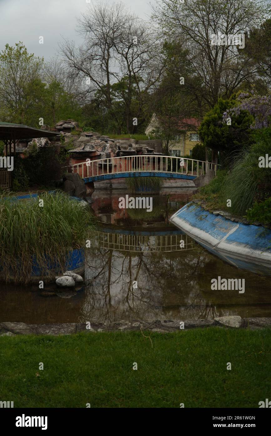 A scenic wooden bridge spanning a peaceful stream in a picturesque park surrounded by lush ...