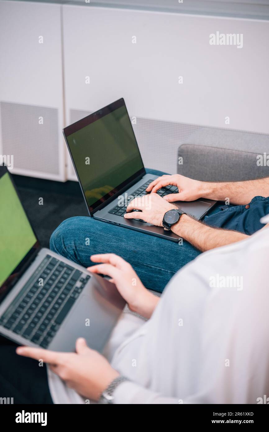Two people using laptops while seated on a cozy sofa: workspace ...