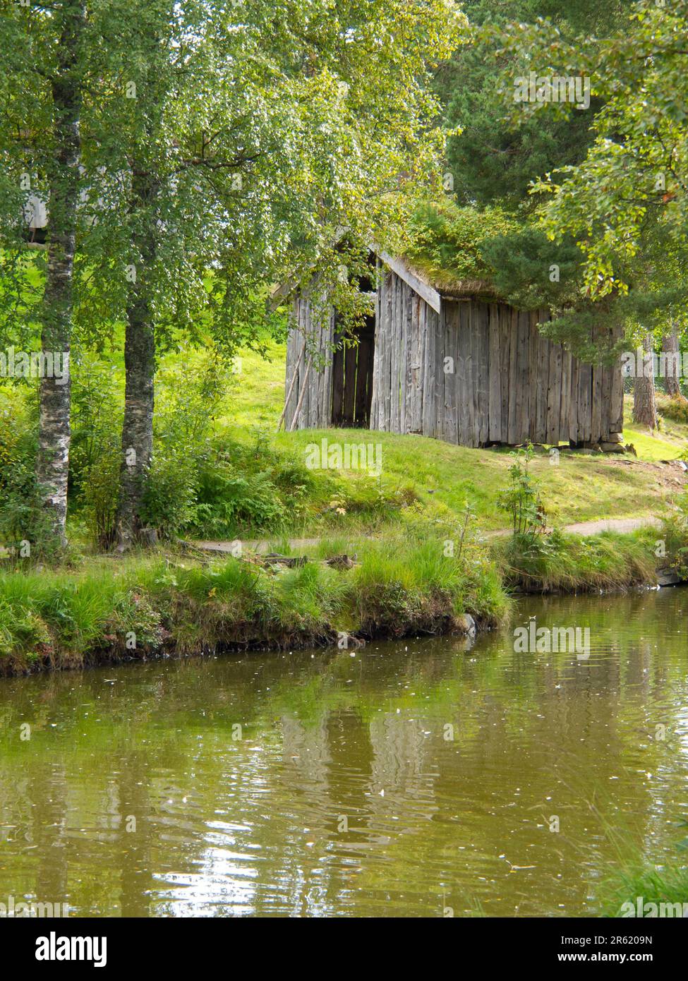 A traditional log cabin is located on the banks of a river surrounded ...