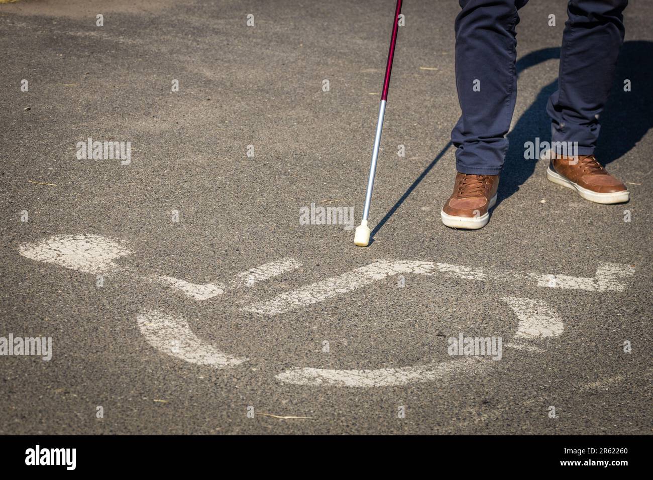 blind person with a cane walking in front of a horizontal sign for ...