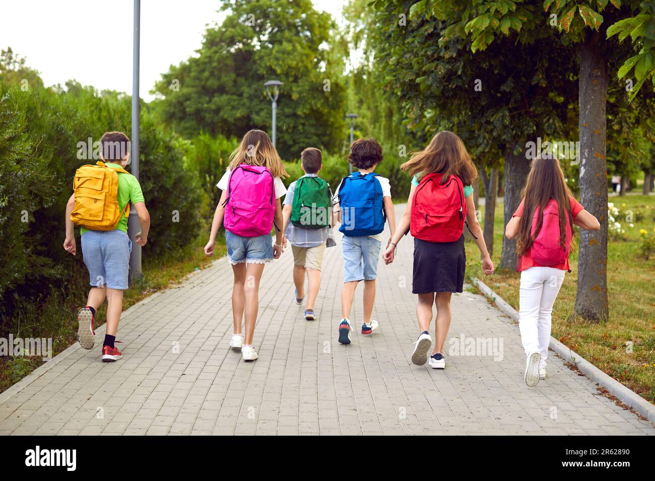 Group of children with backpacks walking along the park path on their ...