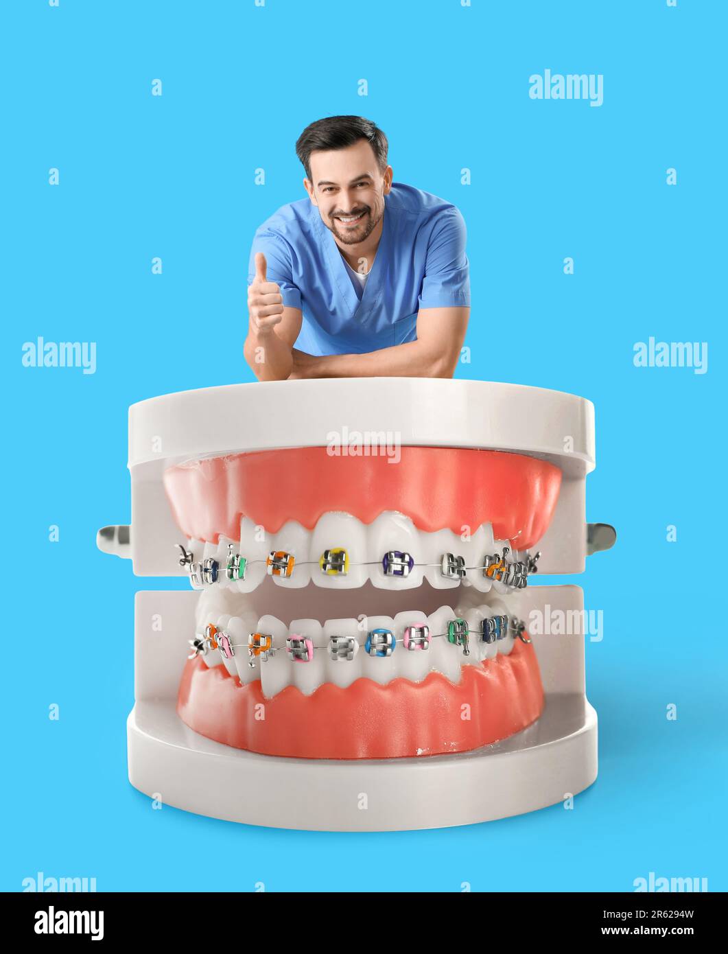 Male dentist and big plastic jaws with braces on light blue background ...
