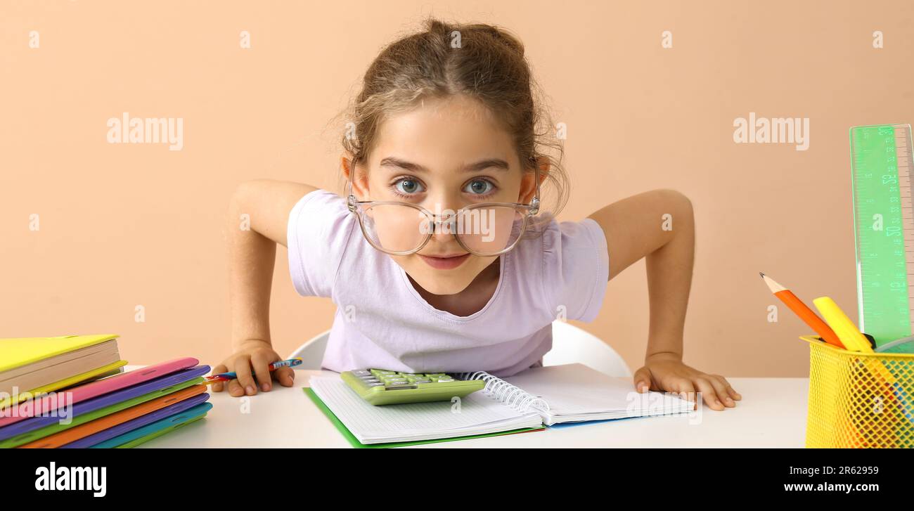 Clever little girl doing homework at table on beige background Stock ...