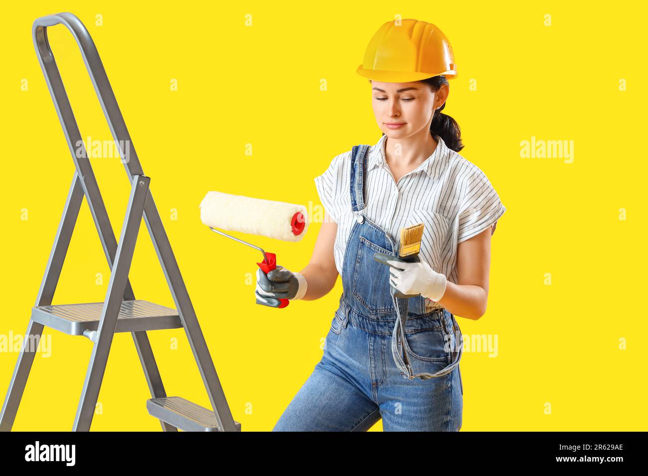Female decorator with paint roller and brush on yellow background Stock ...