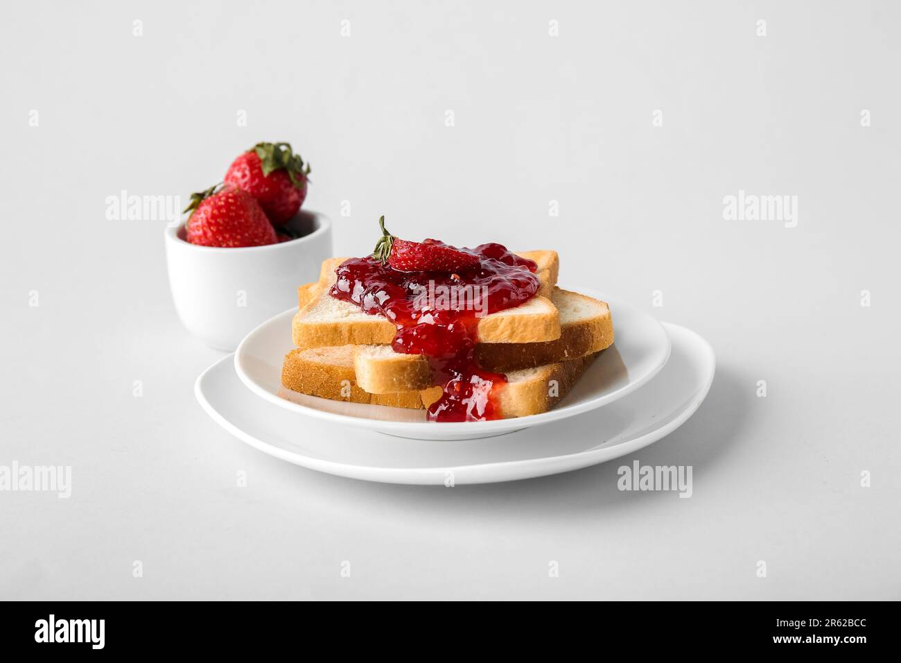 Plates and tasty toasts with strawberry jam on white background Stock ...